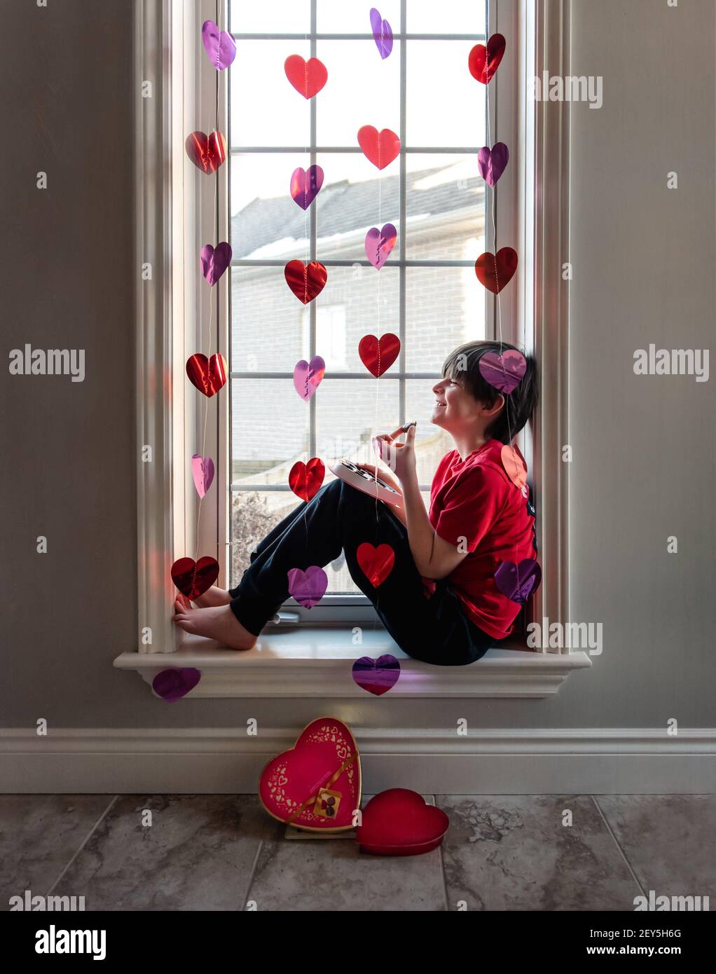 Boy eating chocolates in window decorated with hearts for Valentines ...