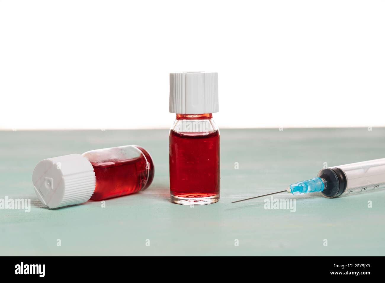 medical vaccine vials with red liquid and syringe over green table and ...