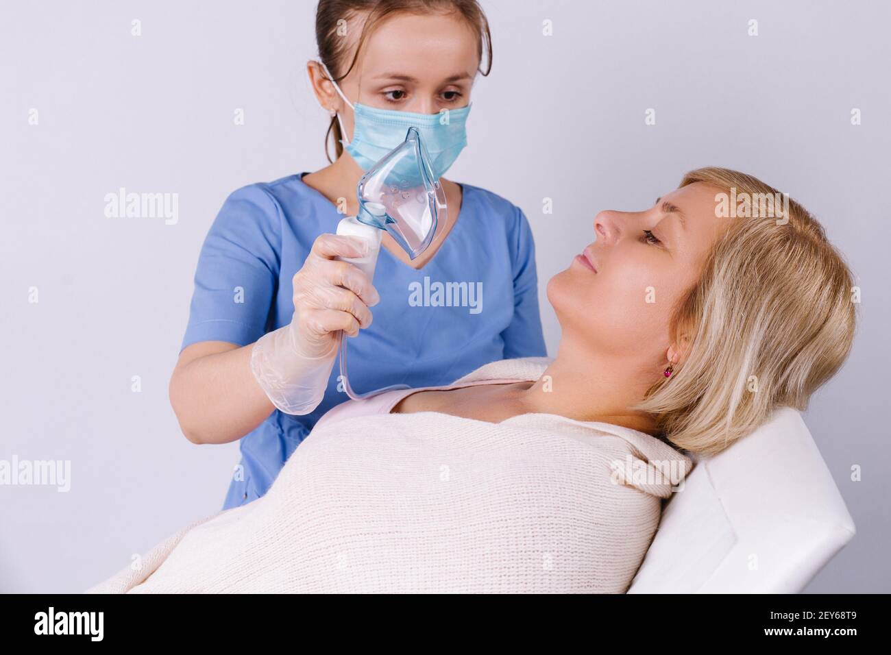 A young nurse in a medical uniform and a mask prepares a nebulizer for ...
