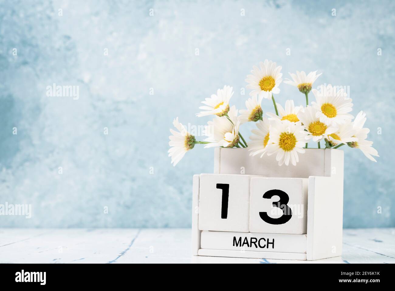 White cube calendar for march decorated with daisy flowers over blue ...