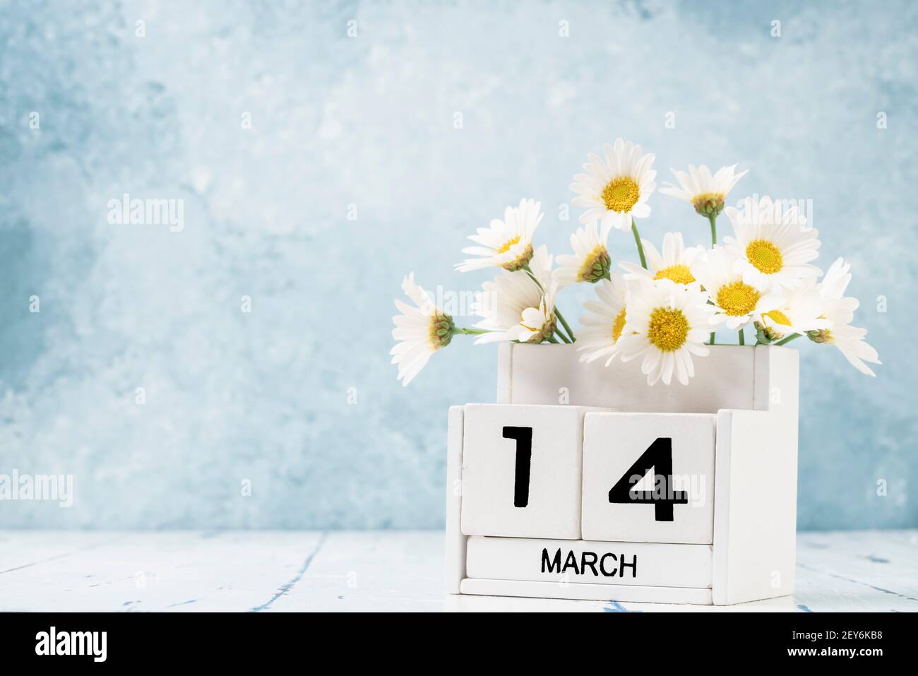 White cube calendar for march decorated with daisy flowers over blue ...