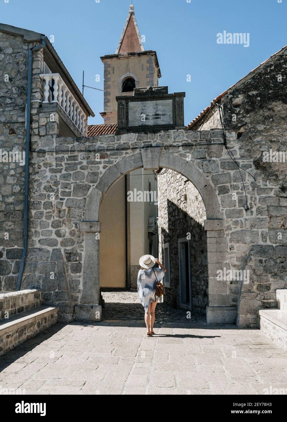 Rear view of woman in summer standing at the entrance to an old town ...