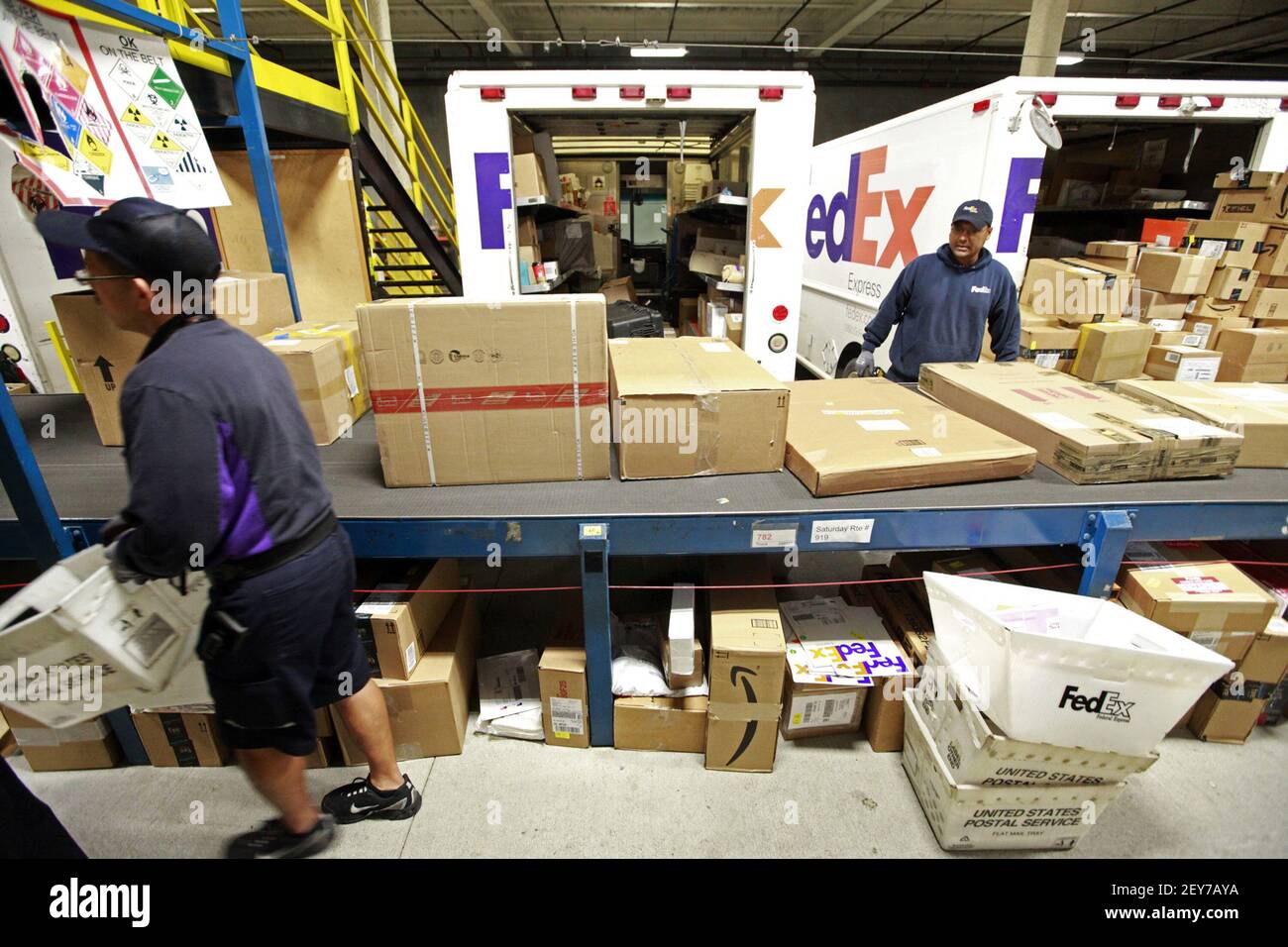 FedEx workers watch for their designated packages slowly moving down a ...