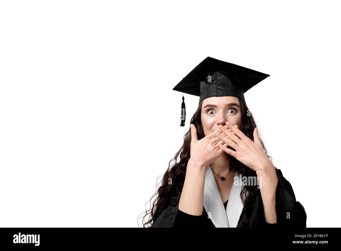Surprised bachelor girl in graduation robe and cap on white background ...