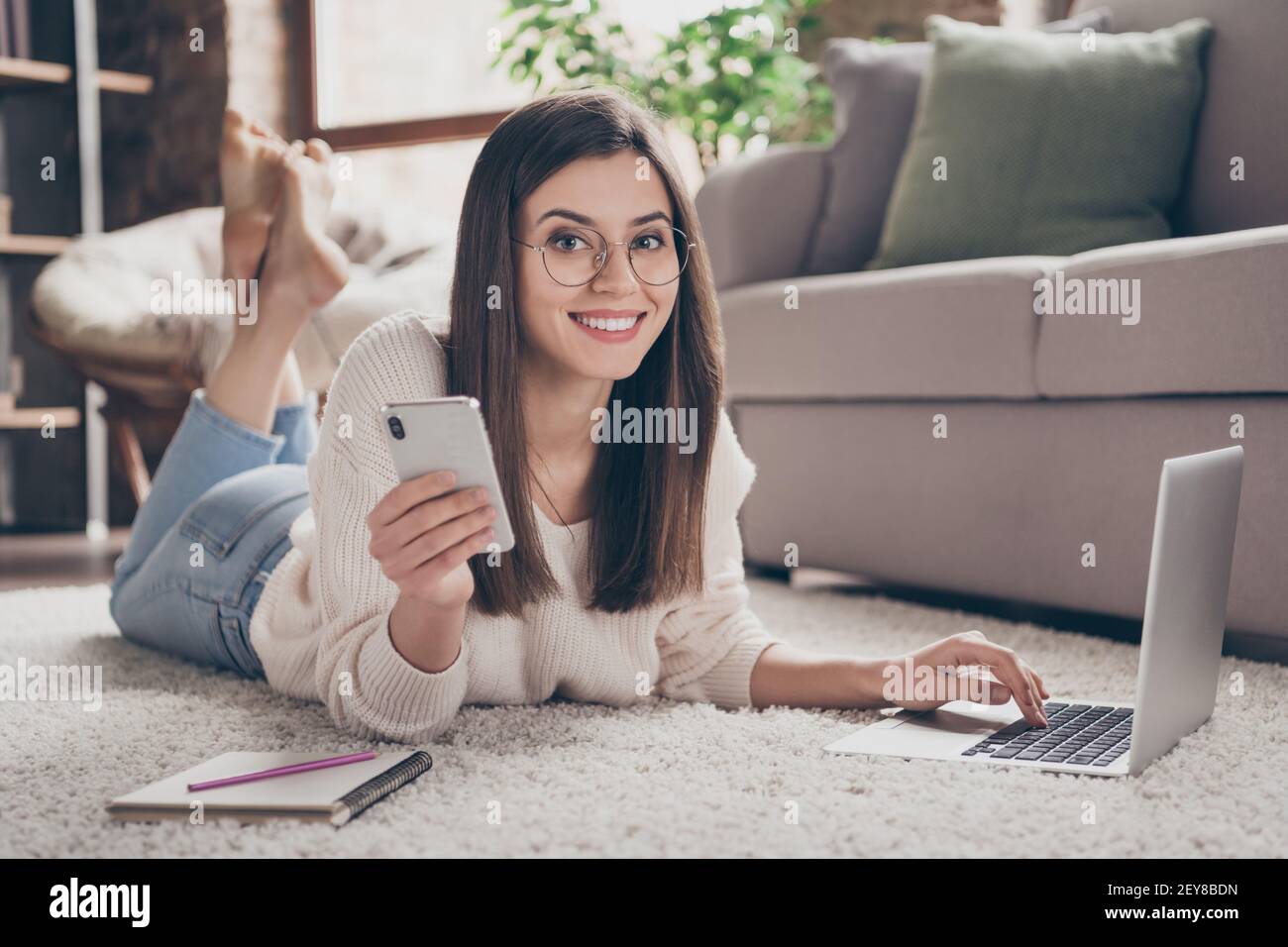 Full size photo of beautiful joyful woman hold phone use laptop lie ...