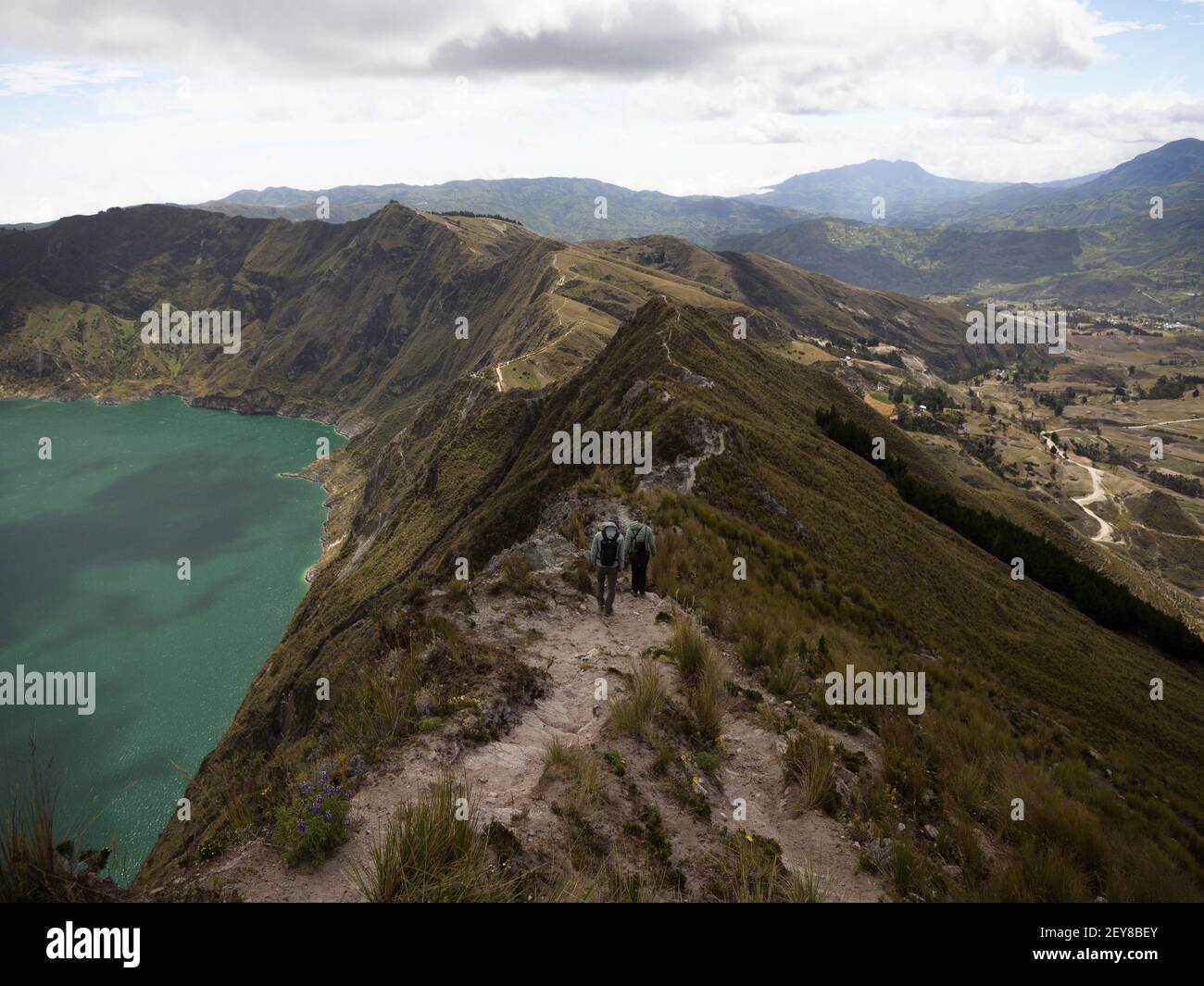 Hikers walking on andean volcano caldera crater lake Quilotoa rim ridge ...