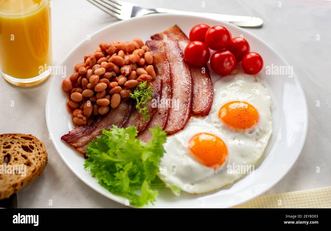 Hearty breakfast with scrambled eggs, bacon, beans, cherry tomatoes ...