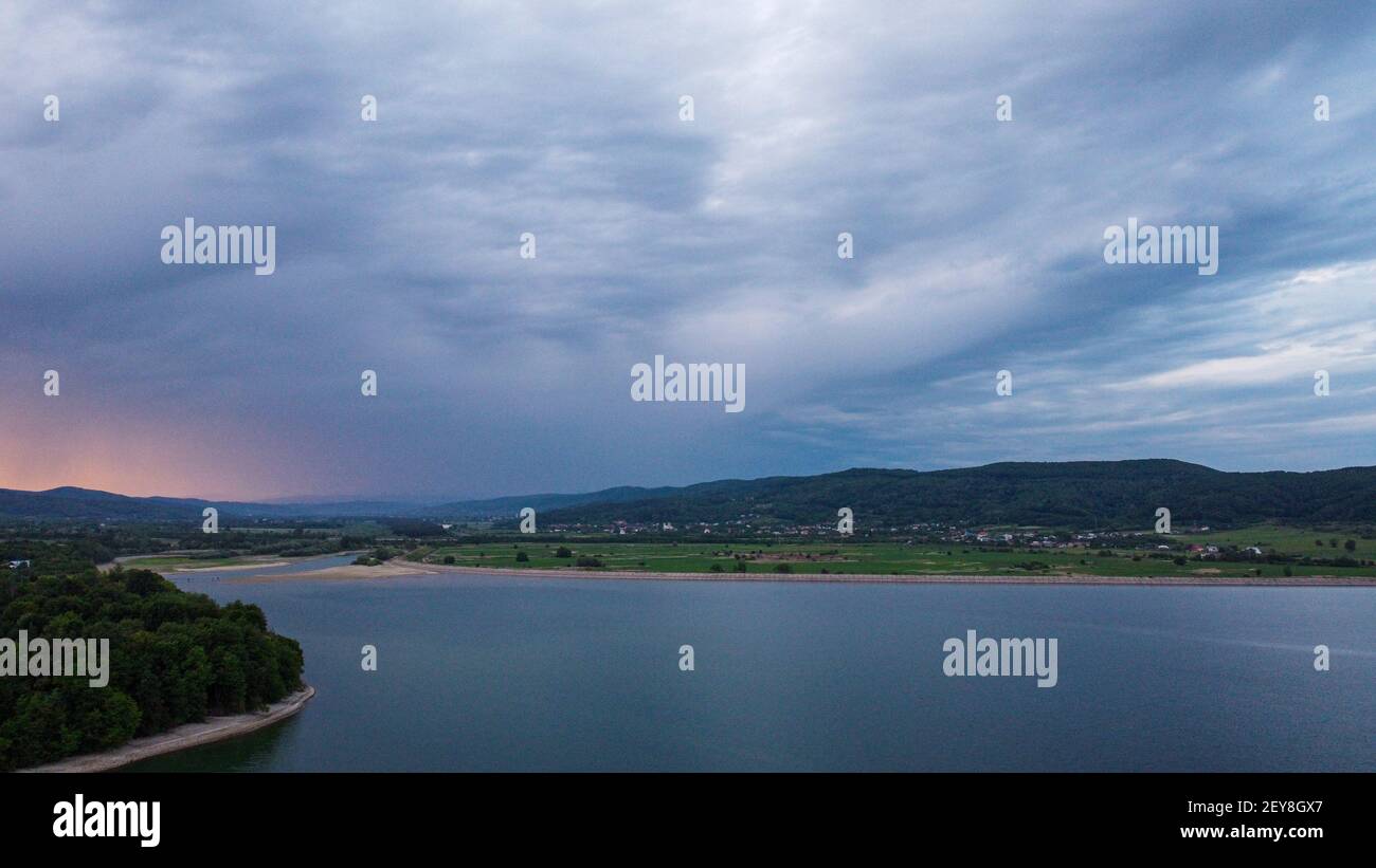 A natural view of a calm river and a vast landscape under a cloudy sky ...