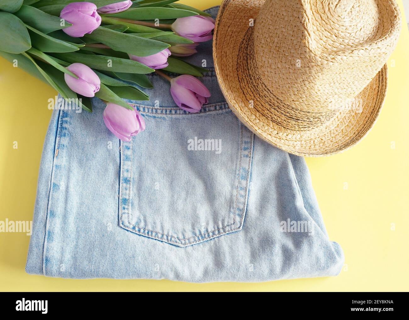 Blue jeans, summer hat and purple tulips flowers on yellow background ...
