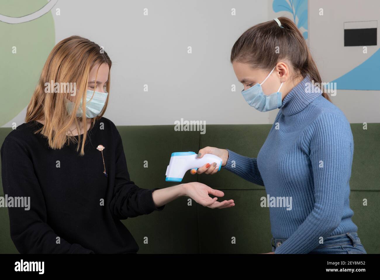Two young women in face masks checking temperature of each other Stock ...