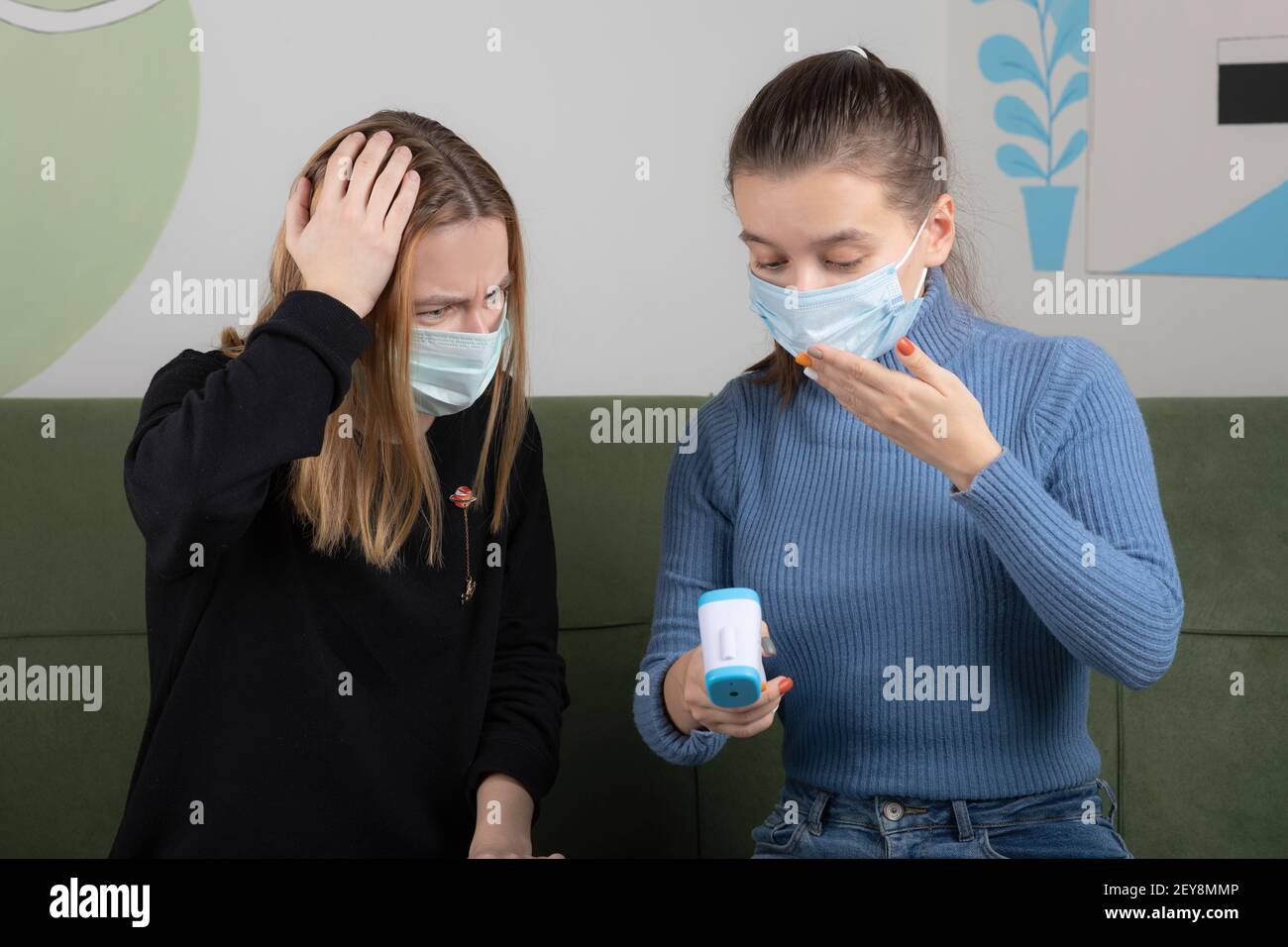 Two young women in face masks checking temperature of each other Stock ...