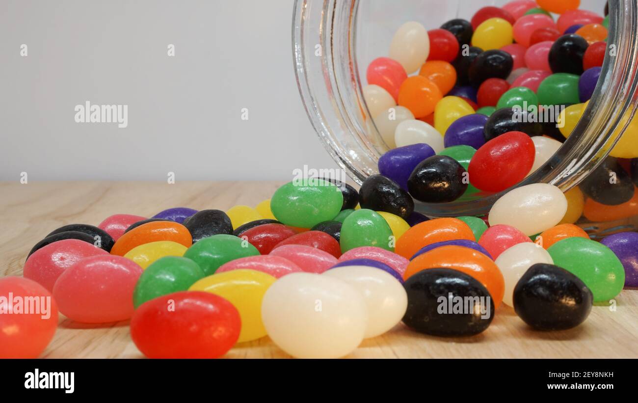 Colorful jelly beans spilling out of a glass jar onto the table. White ...