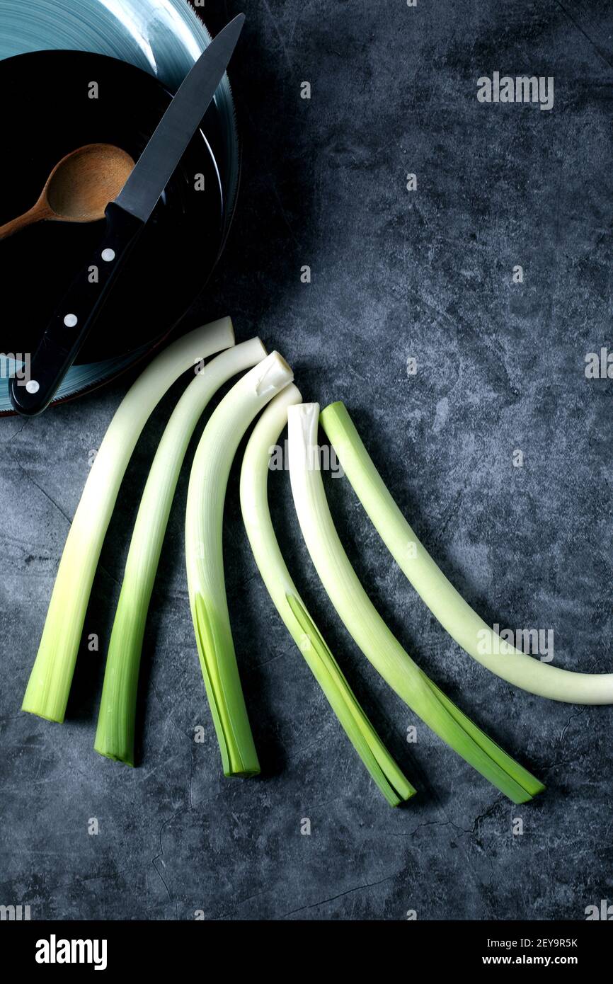 A vertical top view of spring onions on a gray ceramic tile surface ...