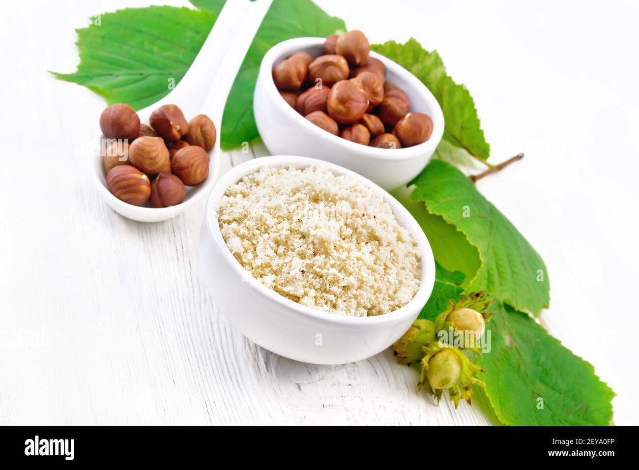 Flour and hazelnuts in two bowls, a spoon with peeled walnut kernels ...