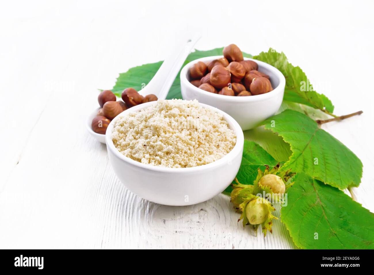 Flour and hazelnuts in two bowls, a spoon with peeled walnut kernels ...