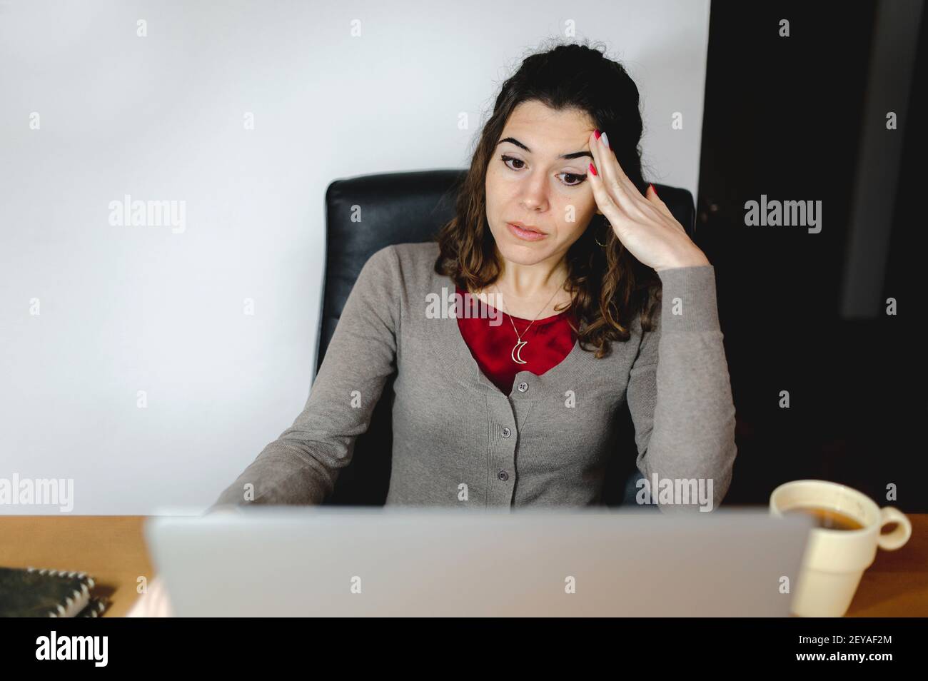 A young tired woman with a thoughtful look looking at the computer ...