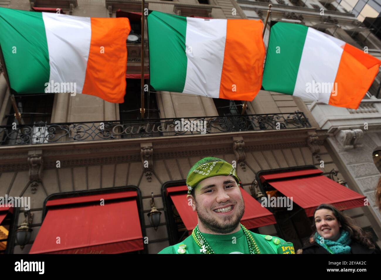 A parade-goer with died greed hair stands under three irish flags ...