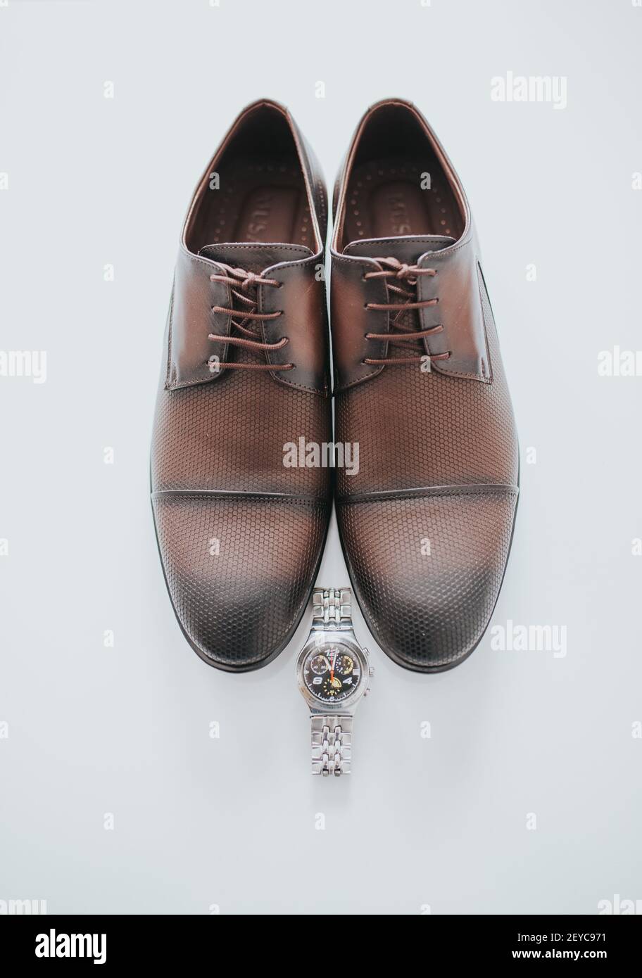 A vertical closeup of a male's shoes and watch on a white background ...