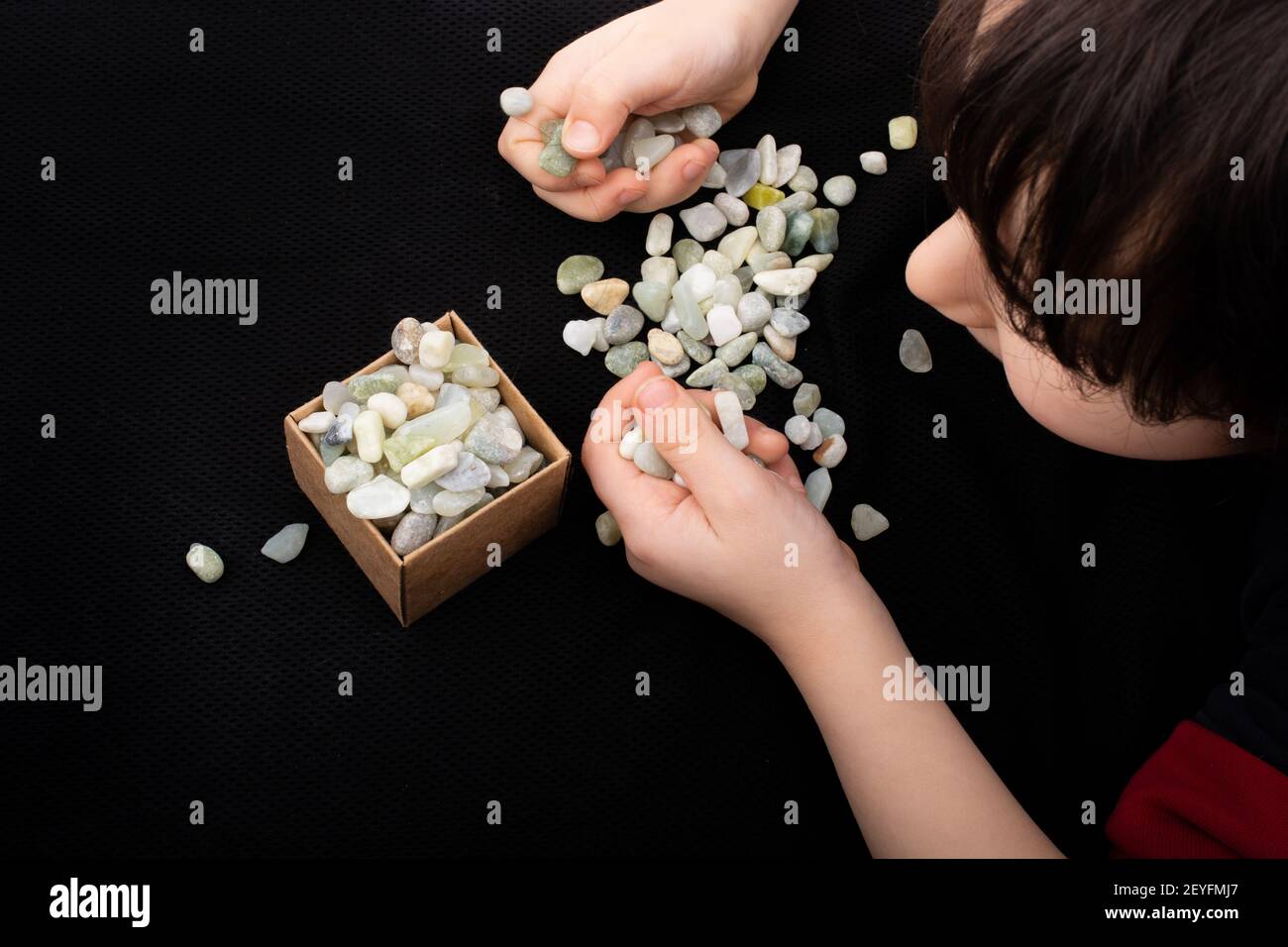 Hand filling the box with stone pebbles gravels on a black background ...