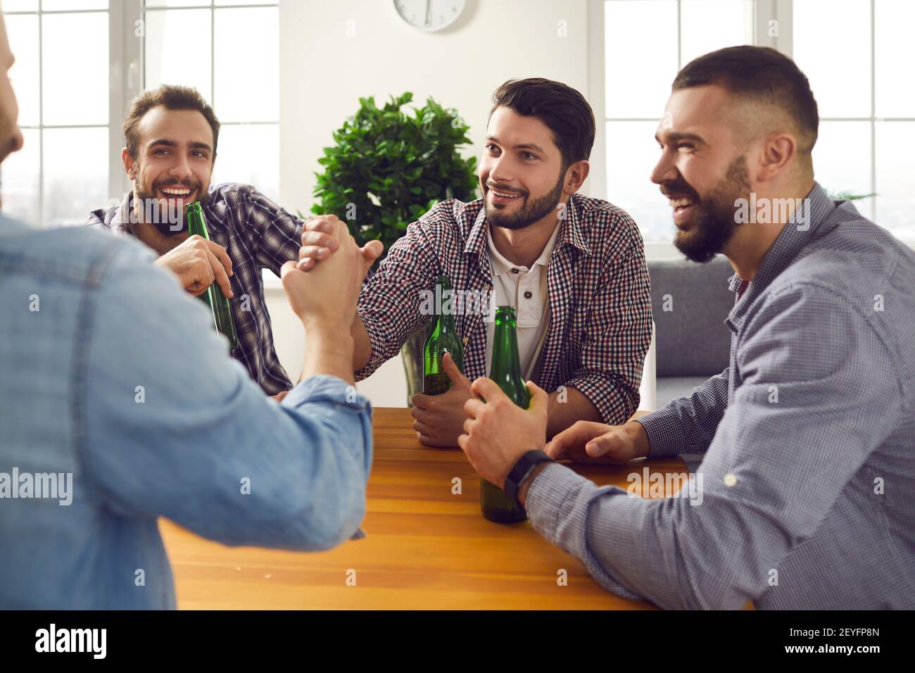 Four smiling men friends sitting with beer at table and competing in ...