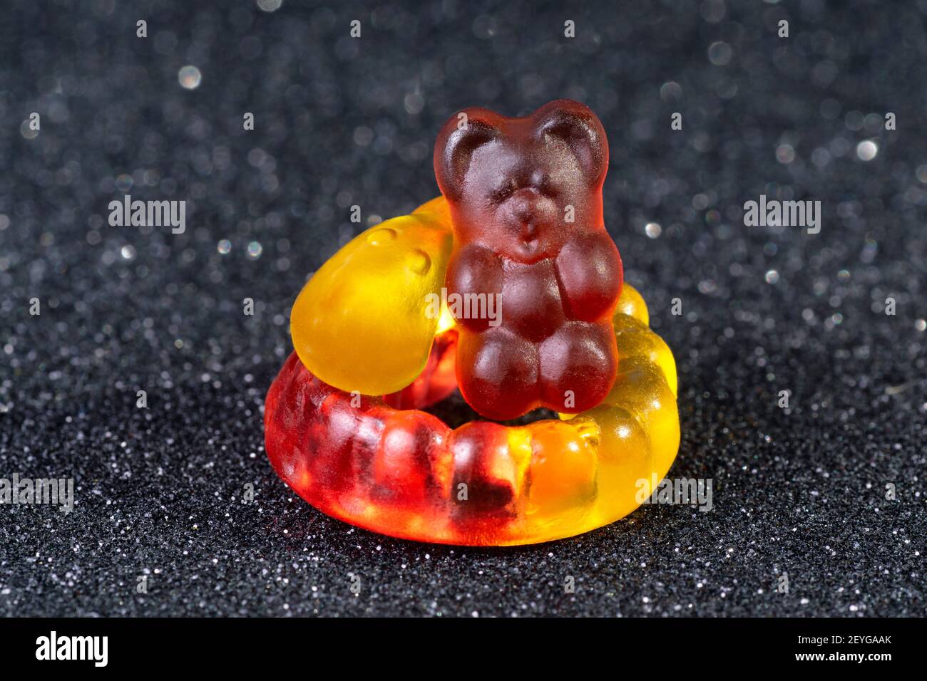 Close-up of a purple gummy bear sitting on a curled yellow-red gummy ...