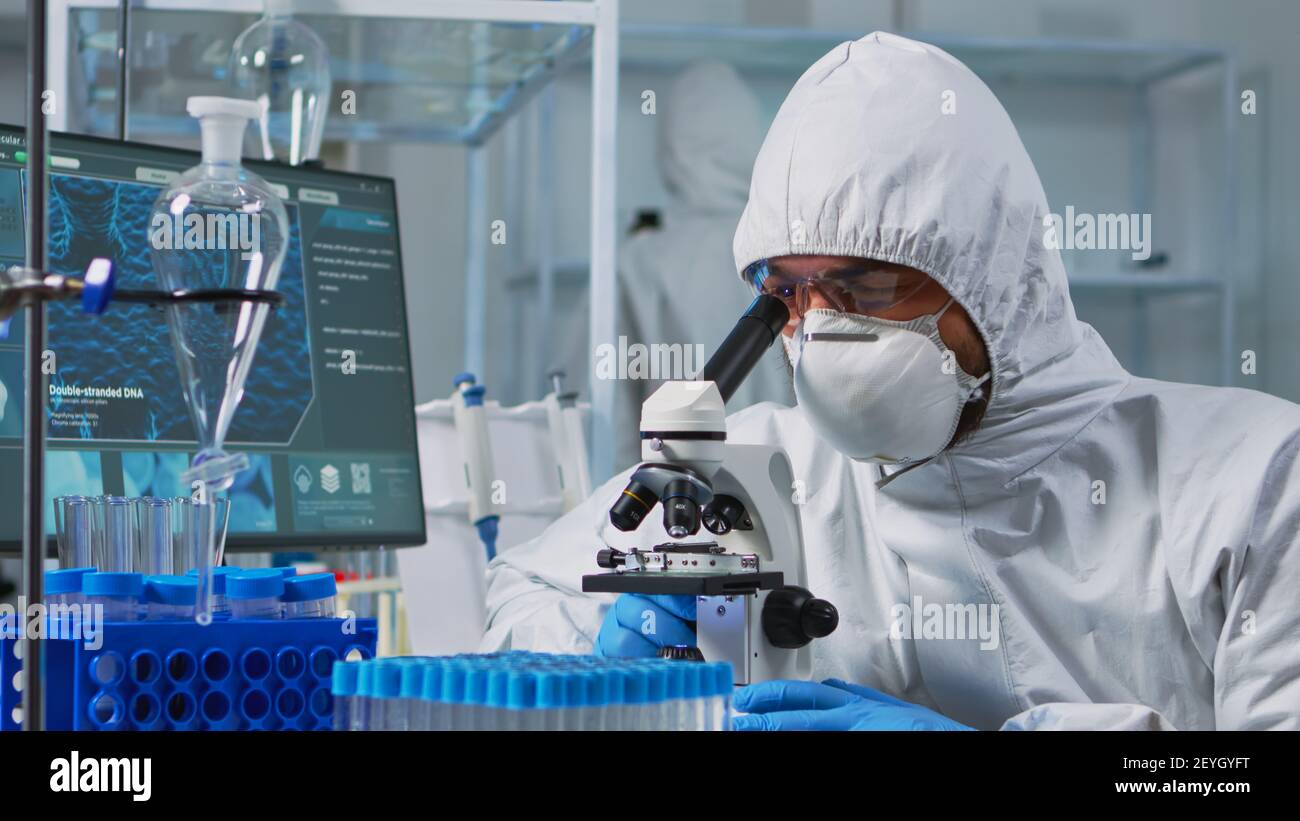 Close up of scientist looking through a microscope wearing ppe suit in ...