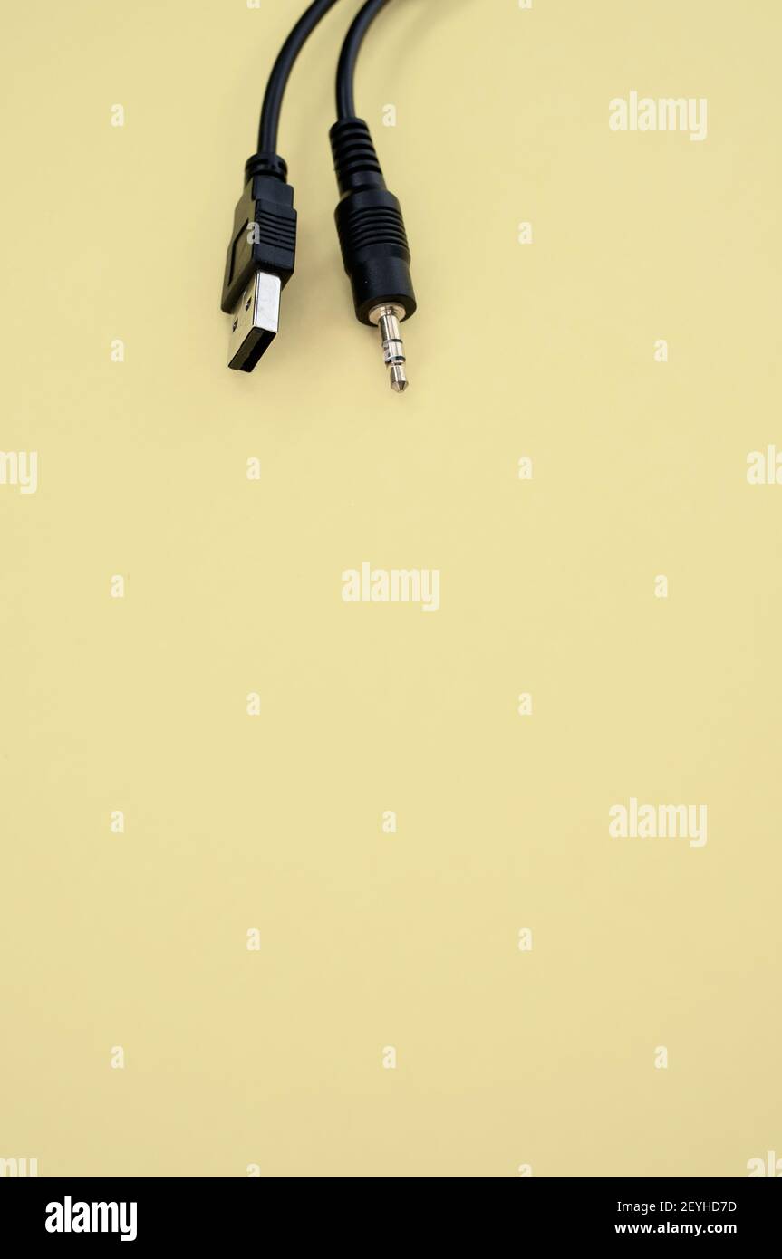 A vertical shot of a wire with a USB end and audio cable on a yellow ...