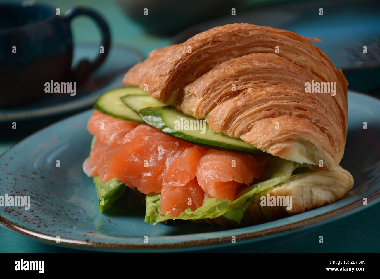Crispy croissant with salmon and lettuce and cucumbers. Tasty breakfast ...