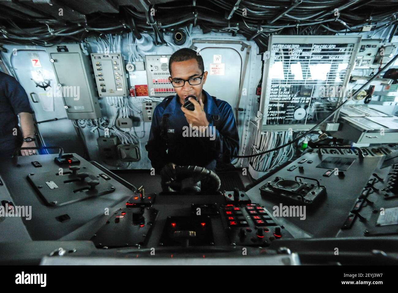 U.S. Navy Seaman Andrew Dowe communicates while steering the amphibious ...