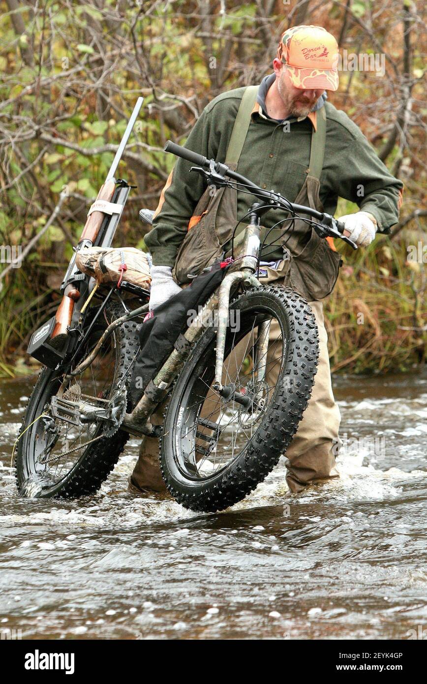Hansi Johnson carries his fat-tire mountain bike across a stream as he hunts near Duluth, Minn ...
