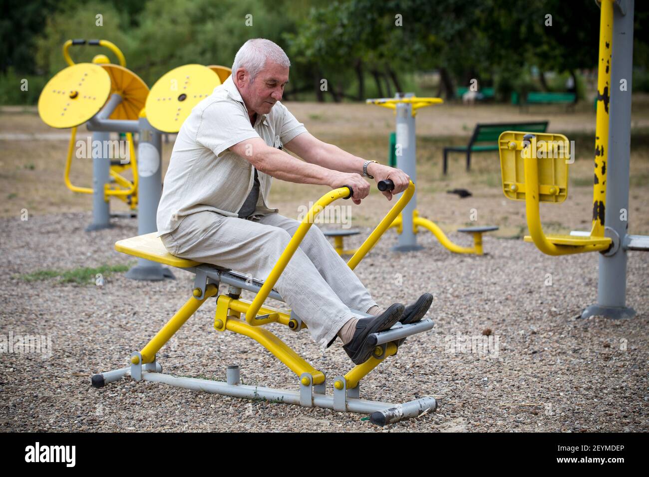 Old man making exercises on outdoor gym against green summer park as a ...