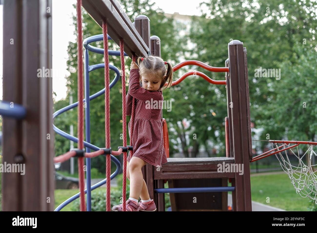 little child girl having fun to climbing rope at playground in summer ...
