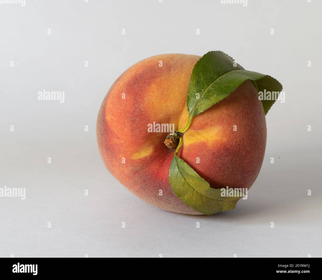 Top of a whole ripe peach turned sideways with a green leaf against ...