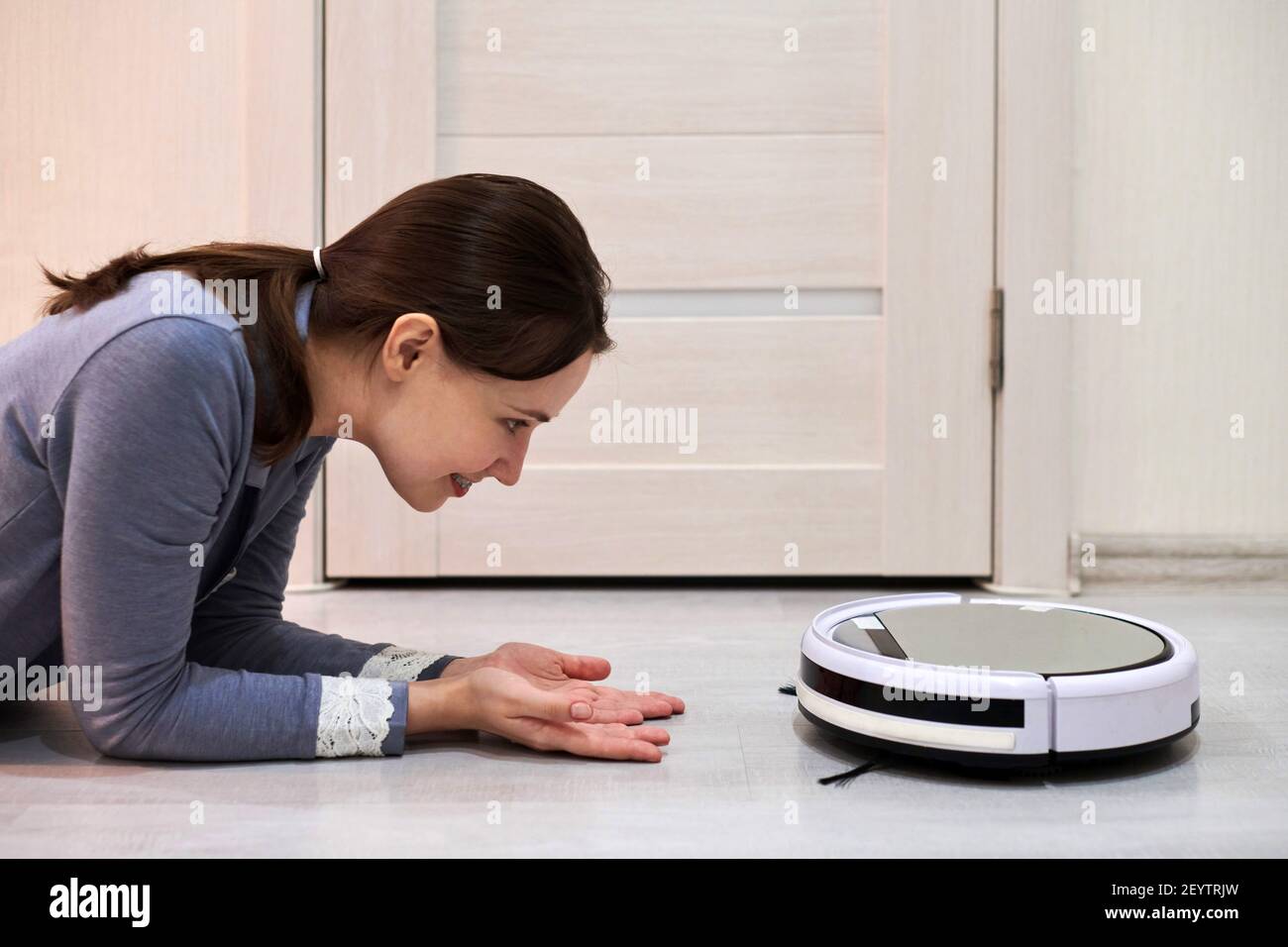 Happy smiling woman lying on floor and looking at robotic vacuum ...