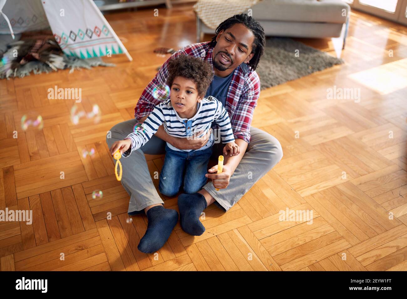 A little boy sitting in the father's lap and making soap bubbles in a ...