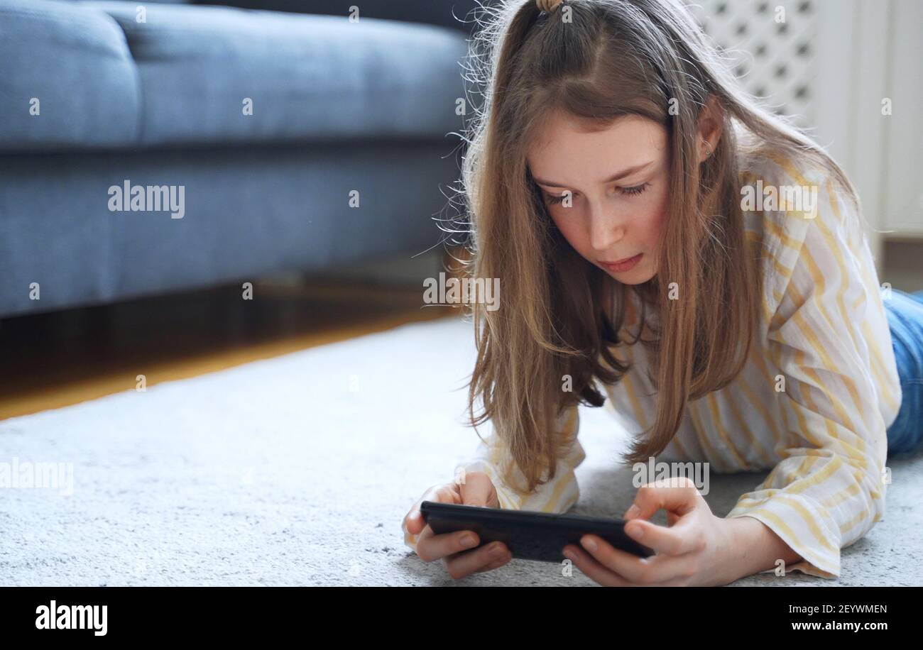 Tween girl with smartphone lying on the carpet Stock Photo - Alamy