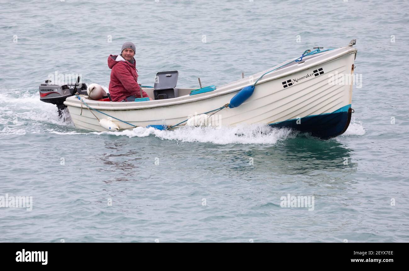 A man in a small wooden boat with an engine heads int the harbour in ...