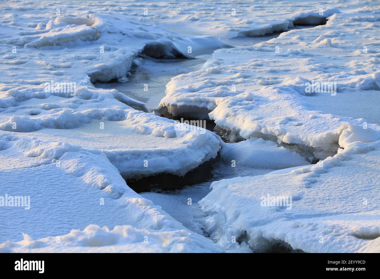 deep winding crack in the ice of a frozen river covered with snow ...
