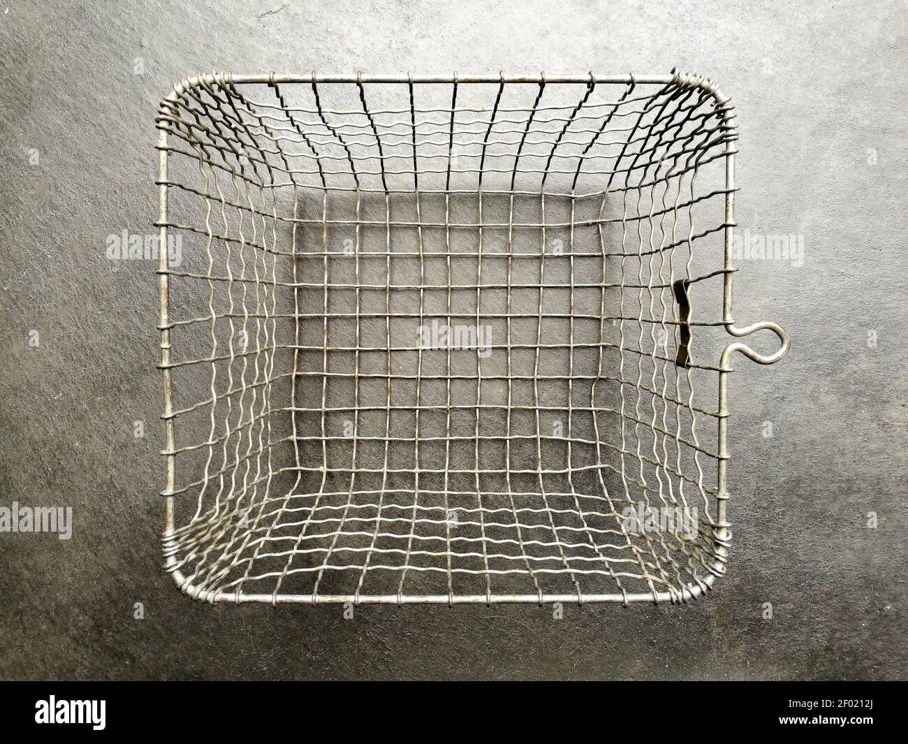 A silver empty wire basket with a square grid structure on a gray ...