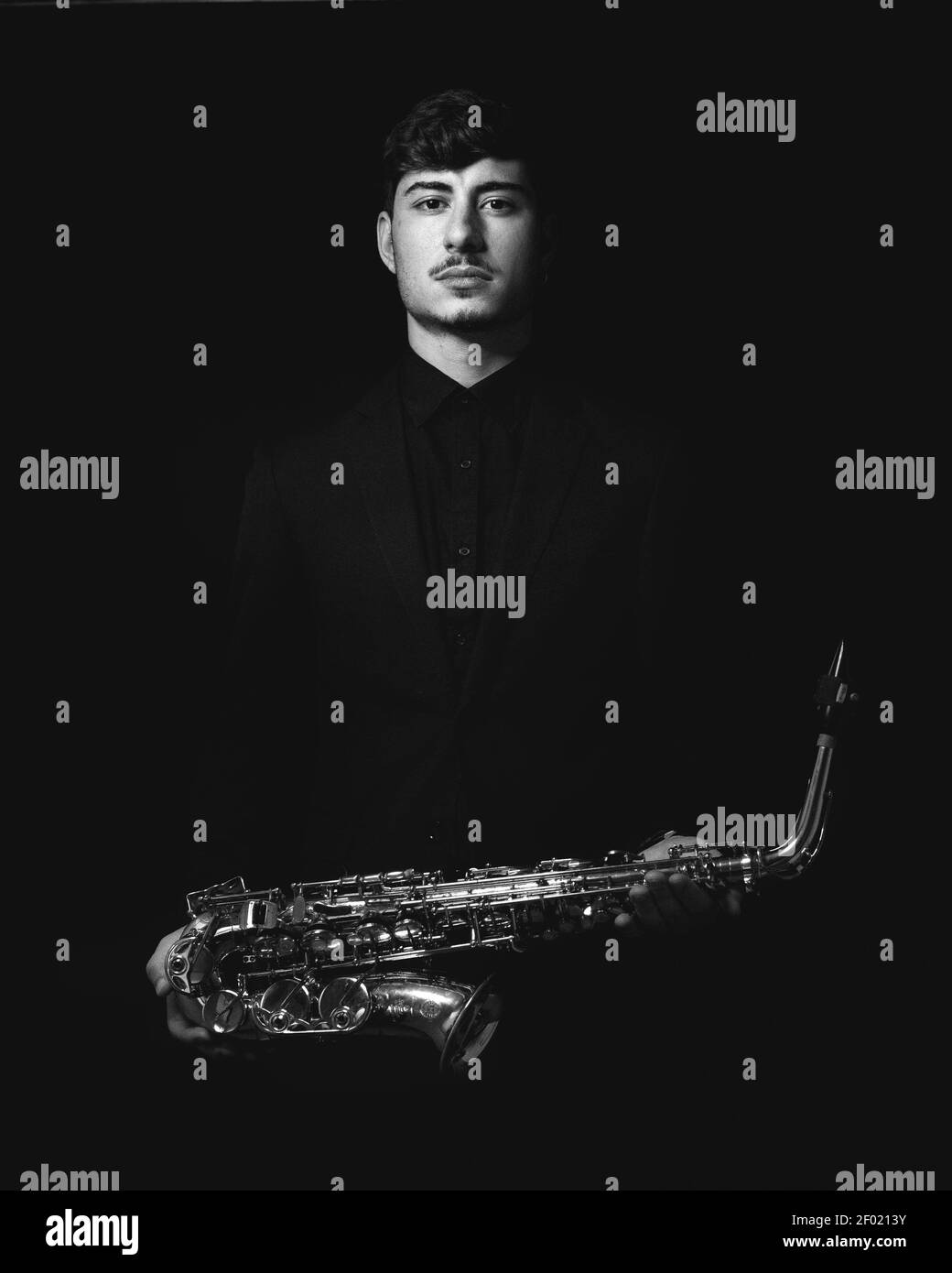A grayscale shot of a cool and handsome guy holding his saxophone on a ...