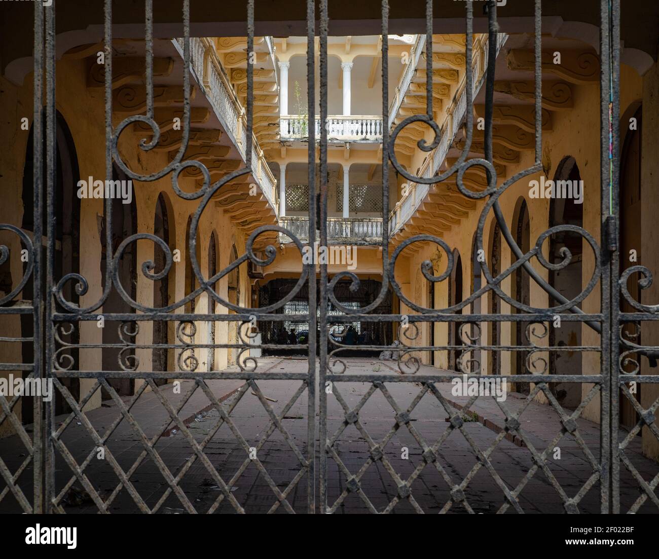 Standing at the locked gates of a yellow and white colonial-style inner ...