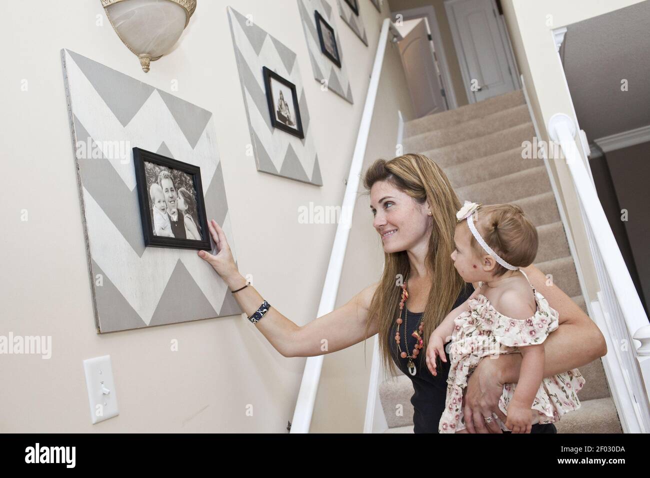 Jennifer Holmes, holding daughter Lorelei, straightens a frame on the display of family ...