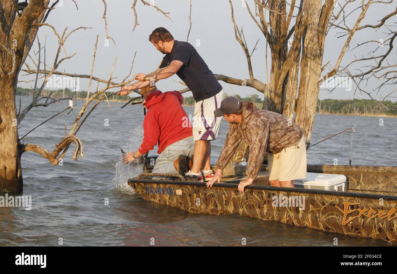 A flathead catfish jumps as Darrell Conrade, left, checks the line on a ...