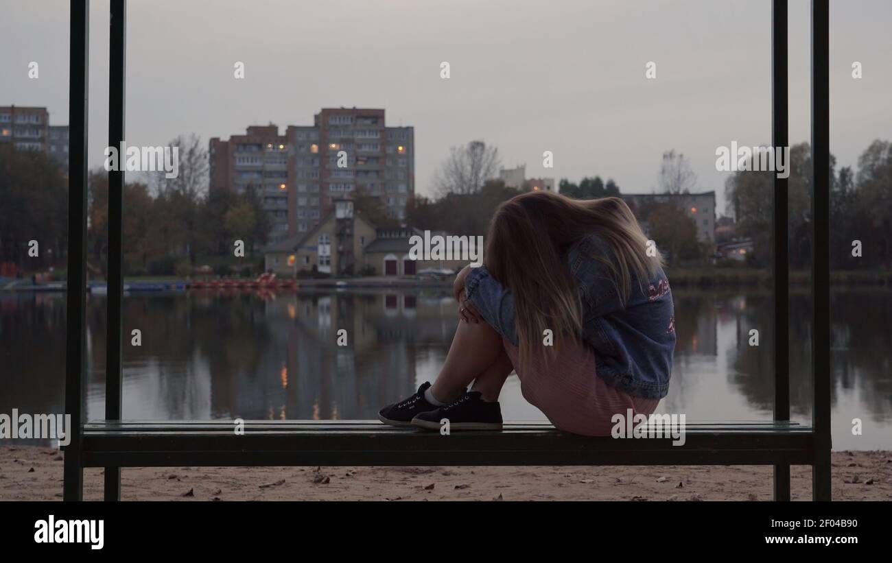 A lonely sad girl sits on a city bench in an autumn evening and cries ...
