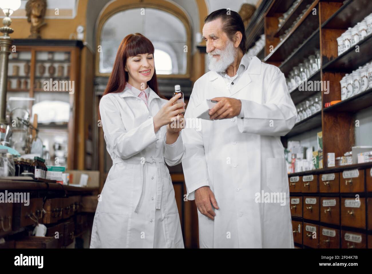 Two pharmacists, senior man and young woman working in vintage old ...