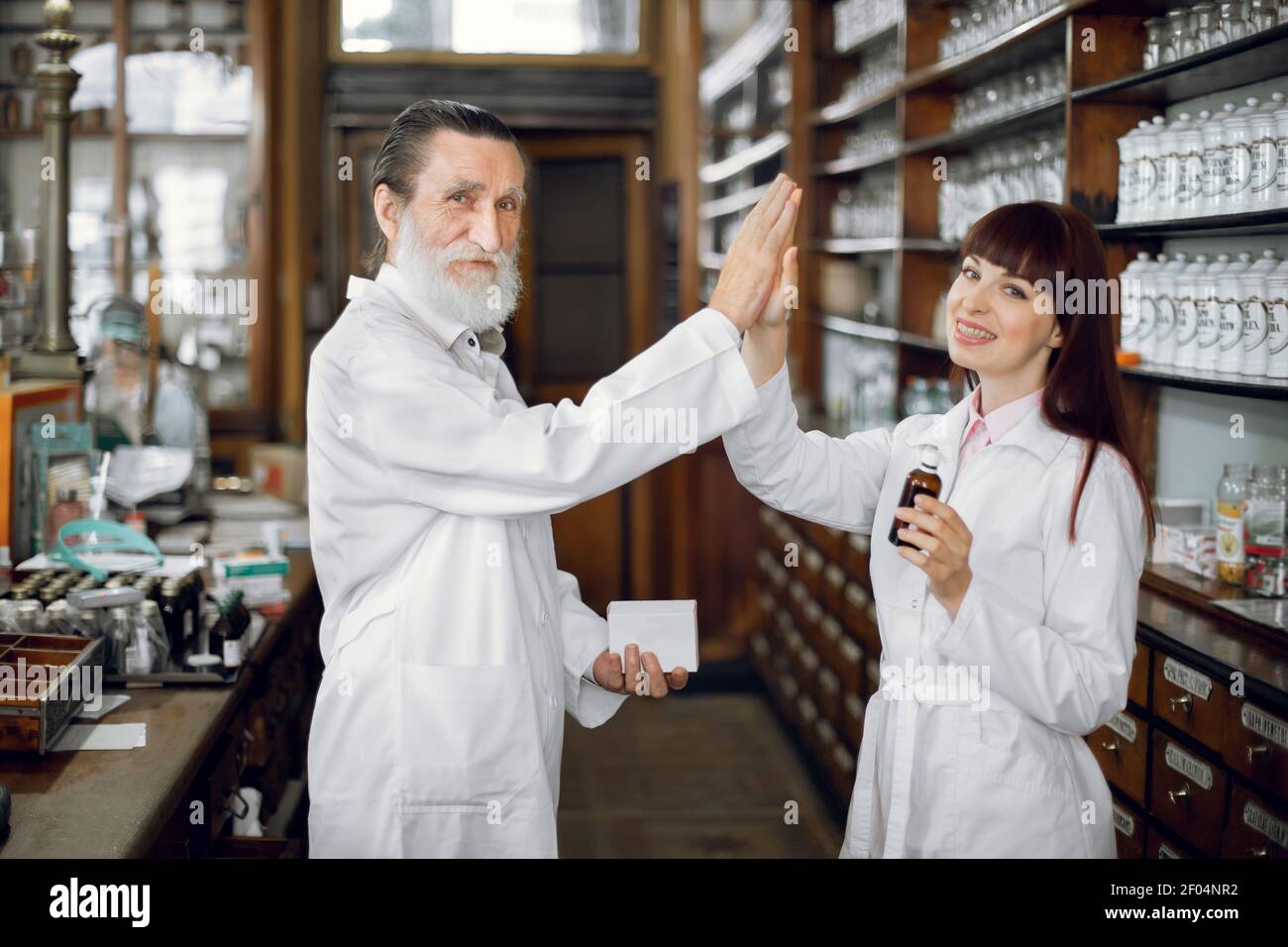Female and male pharmacists in pharmacy. Senior bearded man and young ...