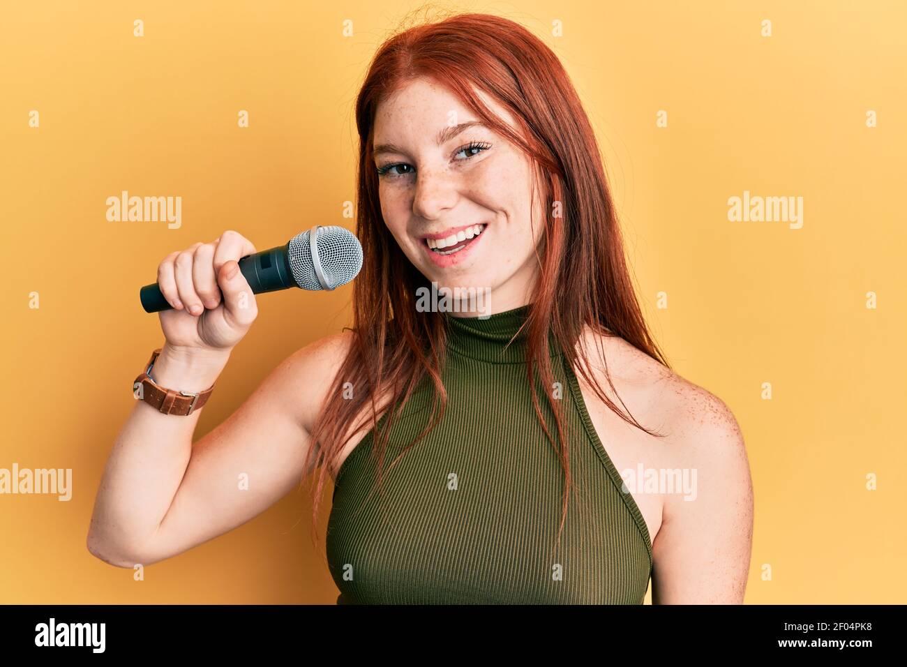 Young red head girl singing song using microphone looking positive and ...