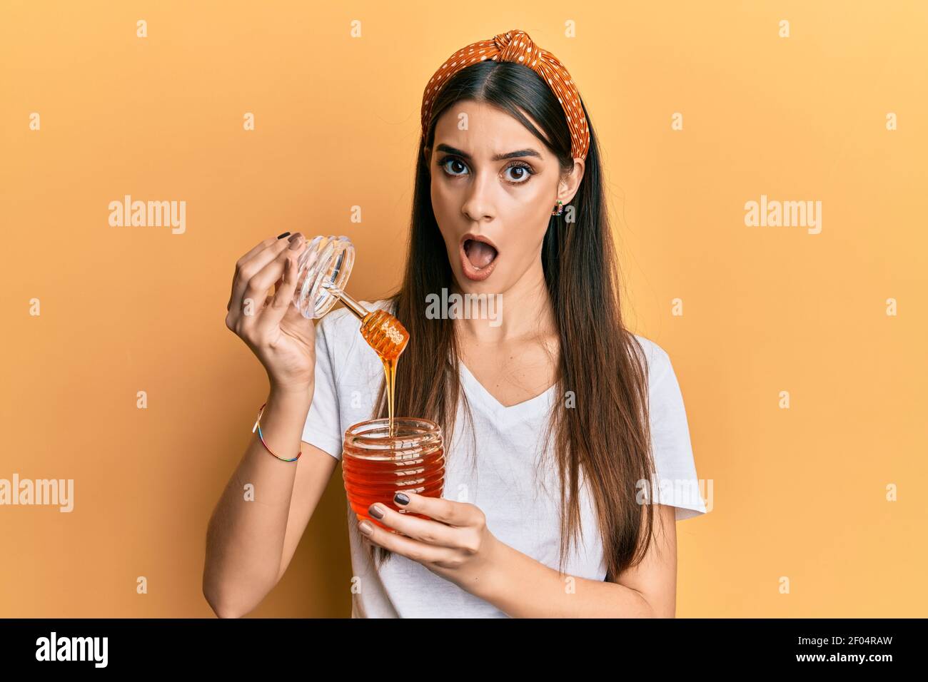 Beautiful brunette young woman holding honey in shock face, looking ...
