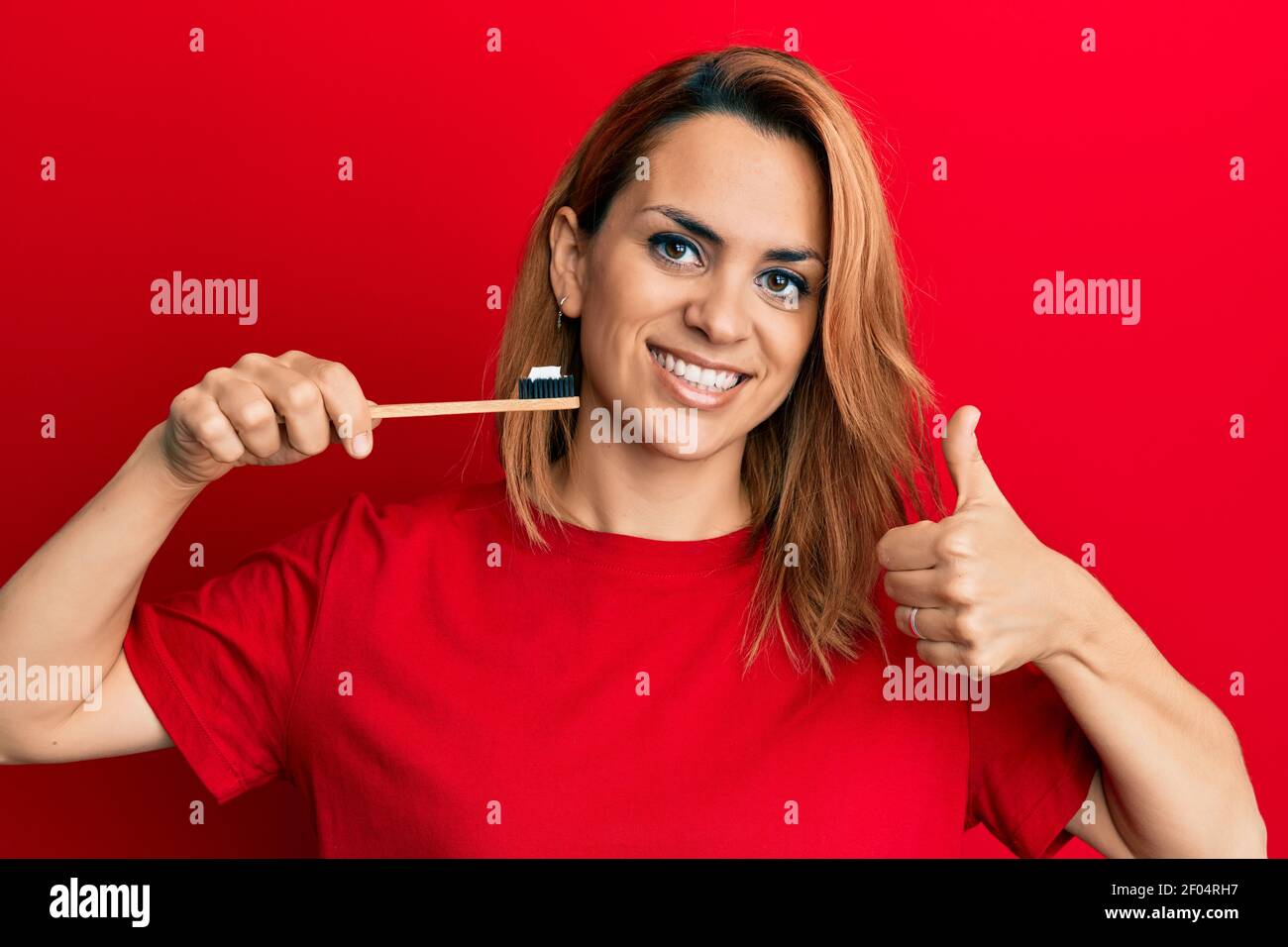 Hispanic young woman holding toothbrush with toothpaste smiling happy ...