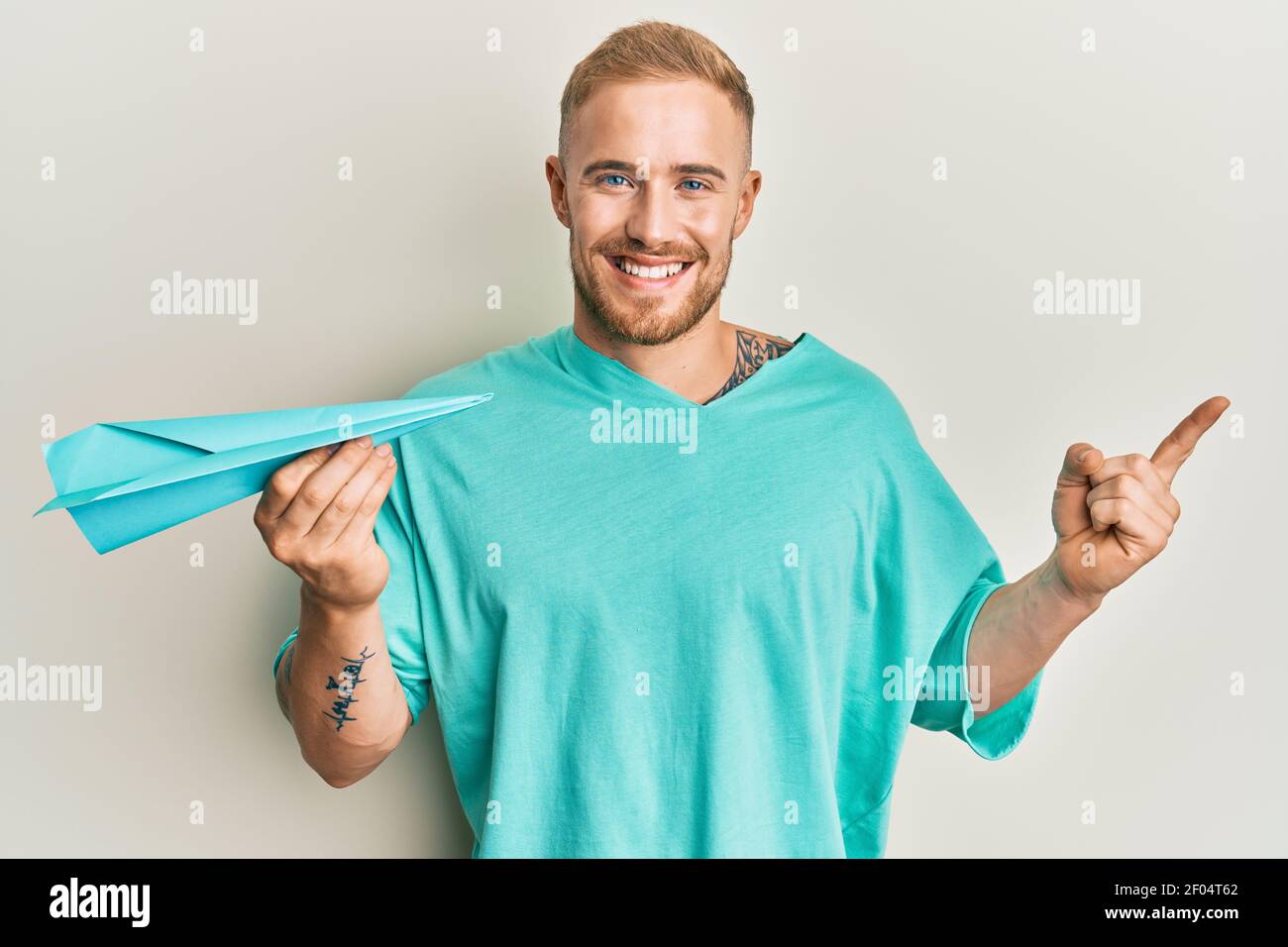 Young caucasian man holding paper airplane smiling happy pointing with ...